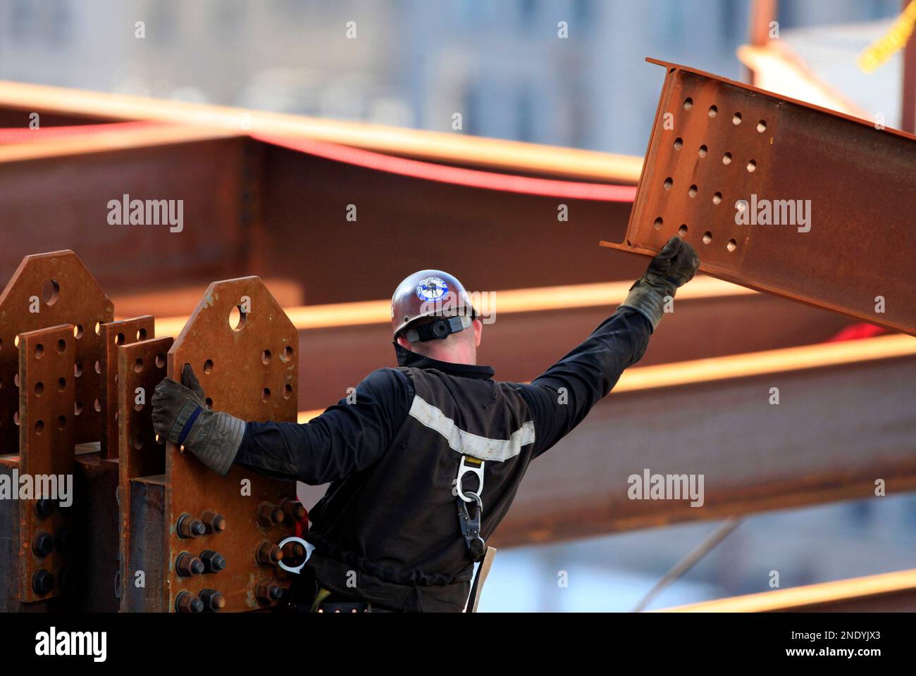 An ironworker guides a steel beam, suspended by a crane, into place at ...