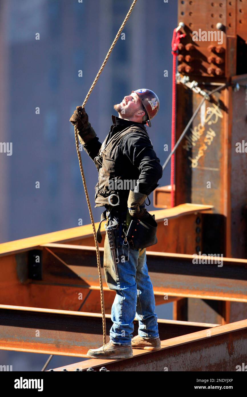 An ironworker guides a steel beam, suspended by a crane, into place at ...