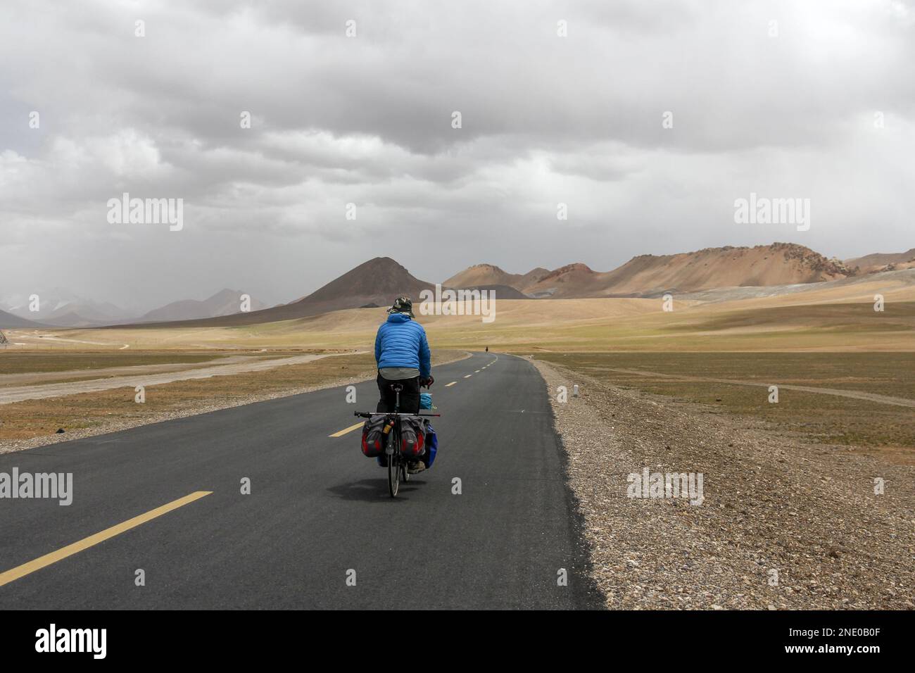 A human riding bicycle on road through desert surrounded by mountains ...