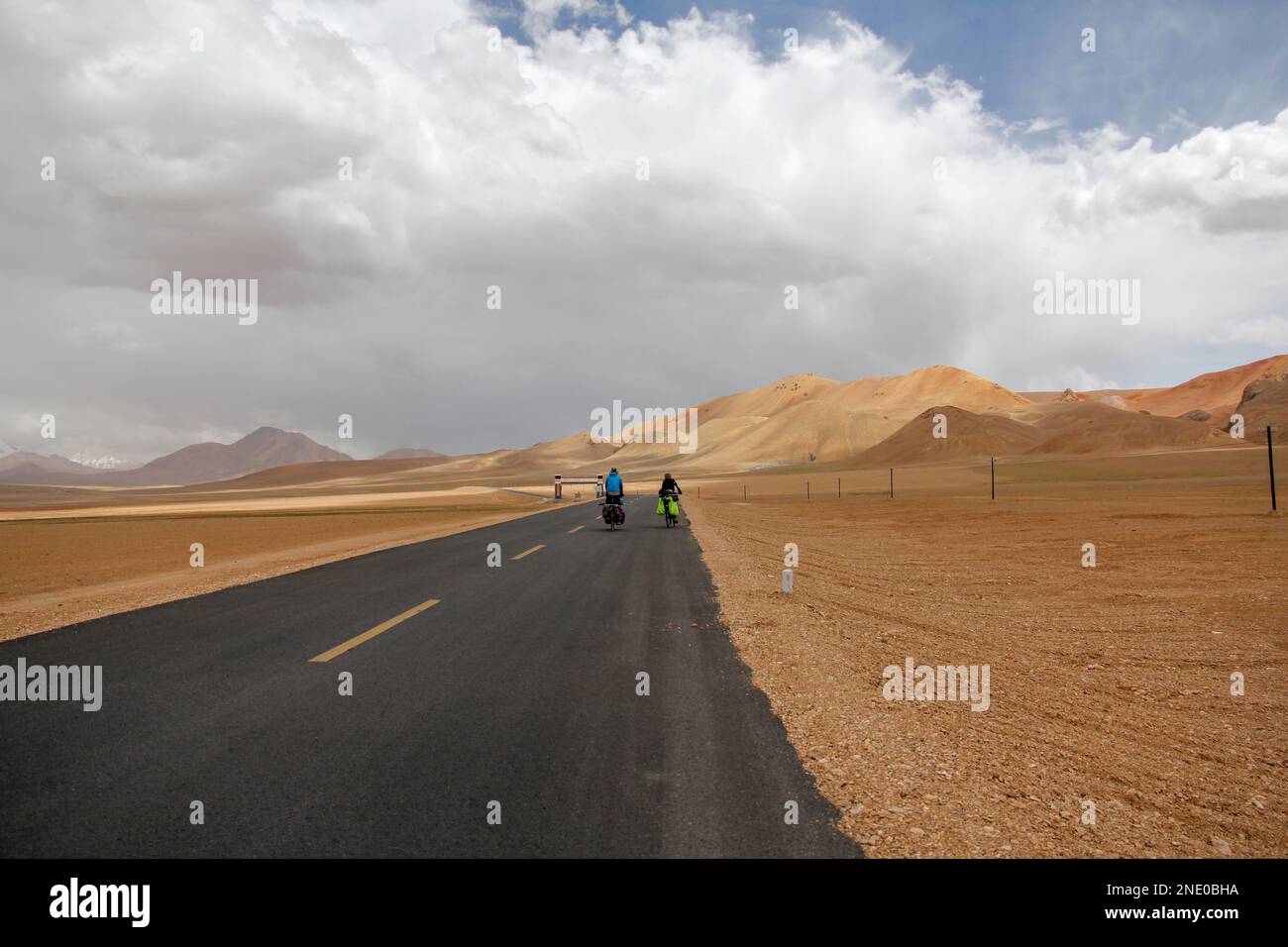 A human riding bicycle on road through desert surrounded by mountains ...