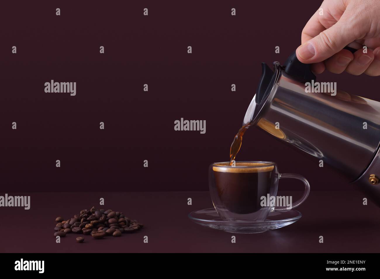 Mans hand pouring fresh hot coffee from a mocha pot into a glass cup ...