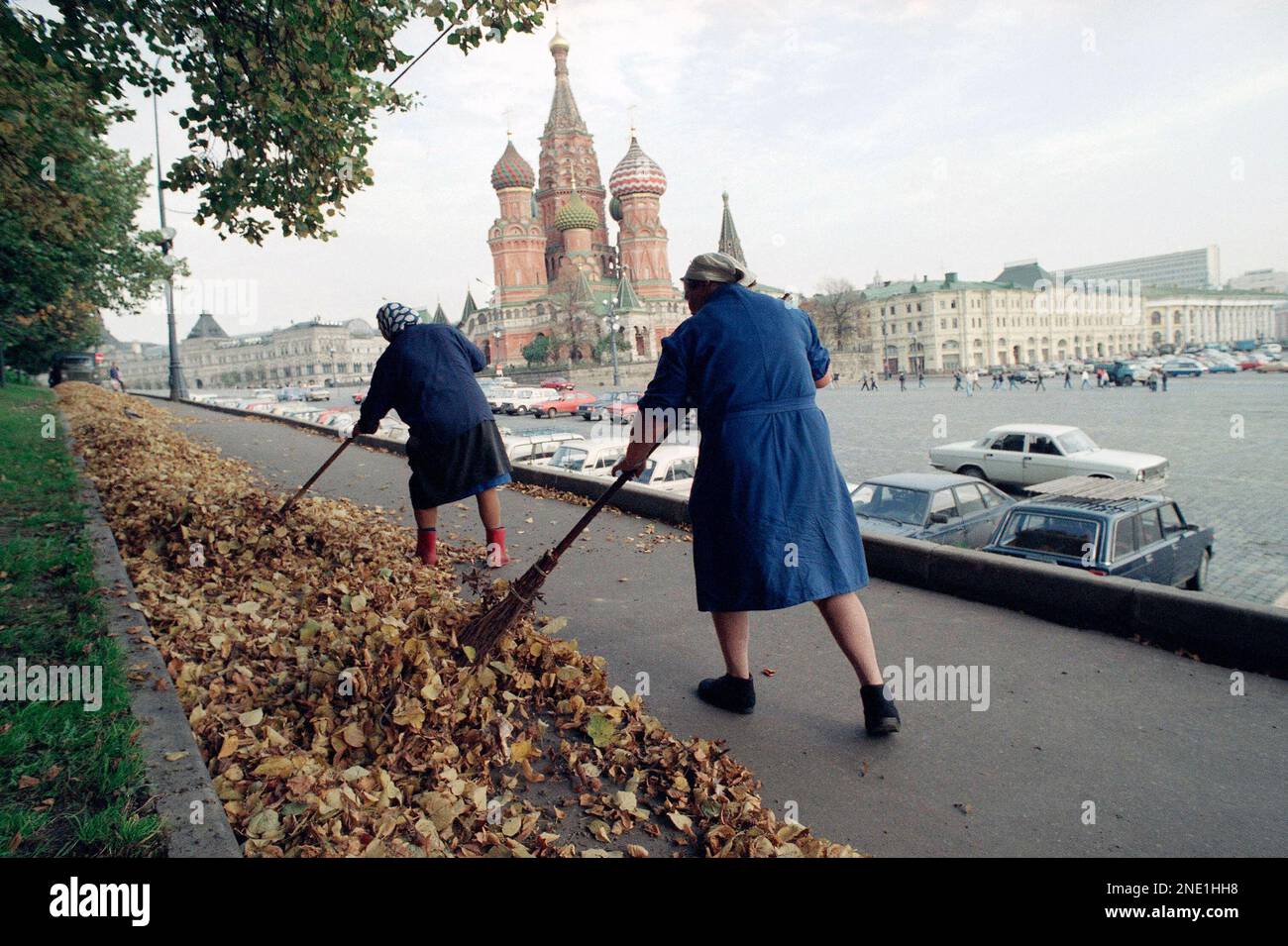 Moscow workwomen sweep fallen leaves from a sidewalk in front of St ...