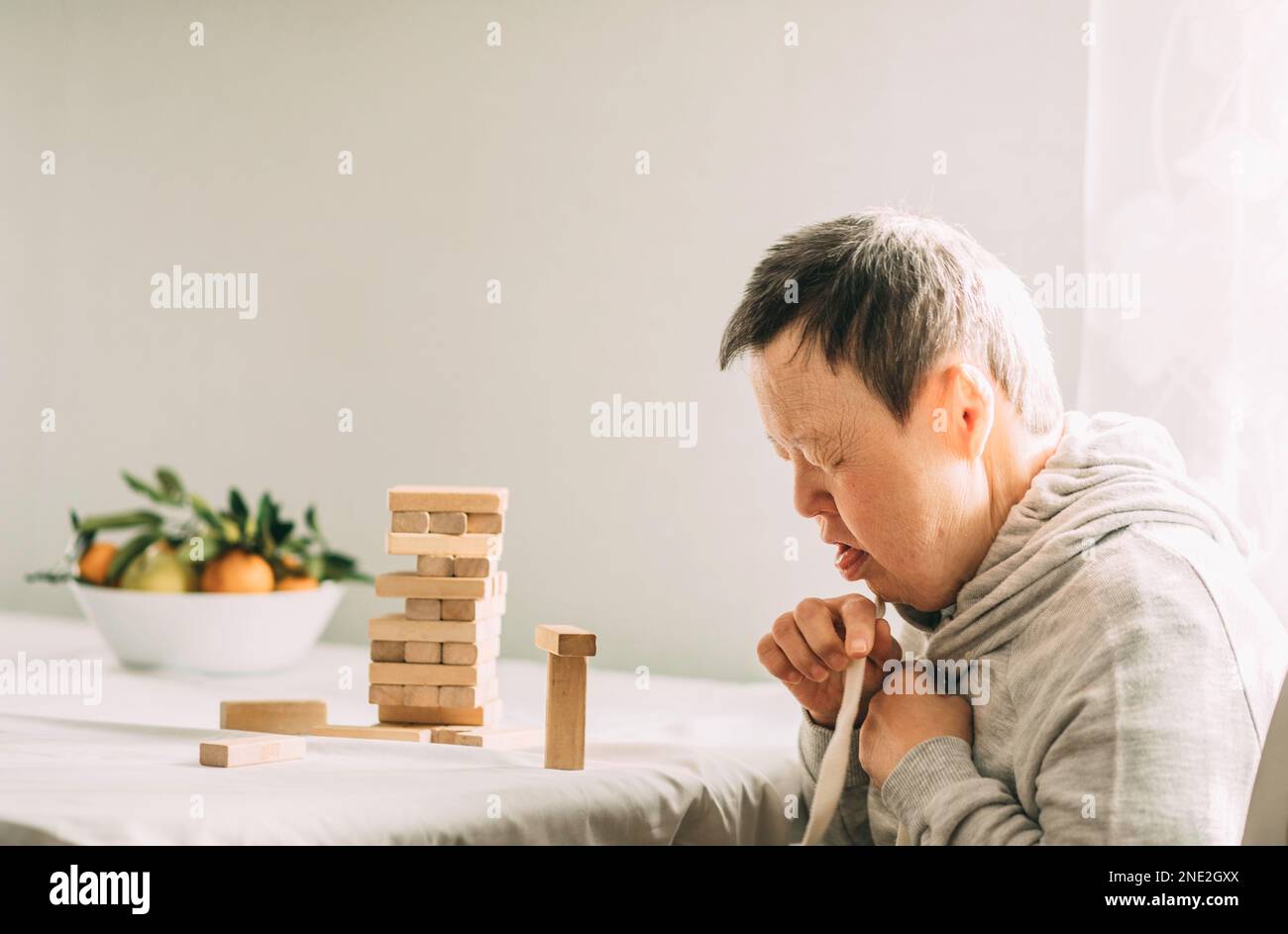 An elderly woman with down syndrome builds towers of wooden toy blocks ...