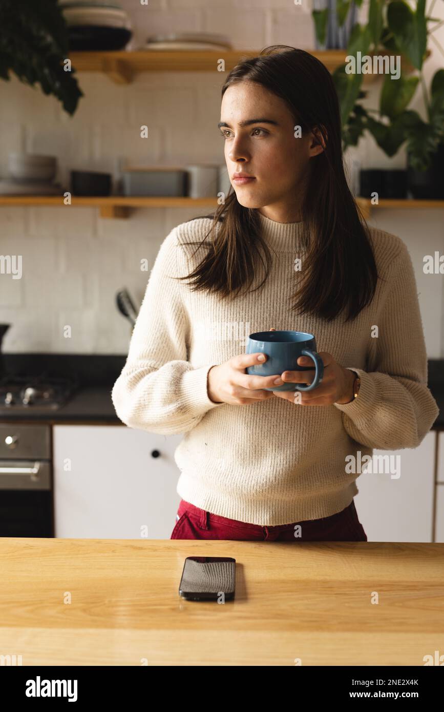 Non-binary trans woman holding a coffee cup in the kitchen at home ...