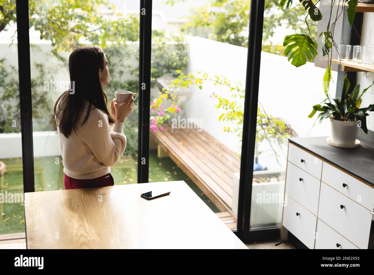 Thoughtful non-binary trans woman holding a coffee cup looking out of ...