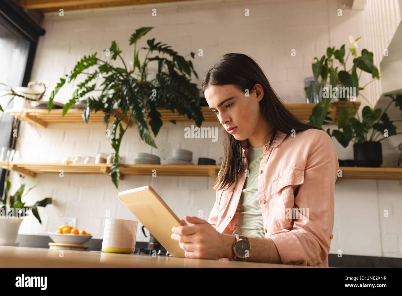 Non-binary trans woman using digital tablet in the kitchen at home ...