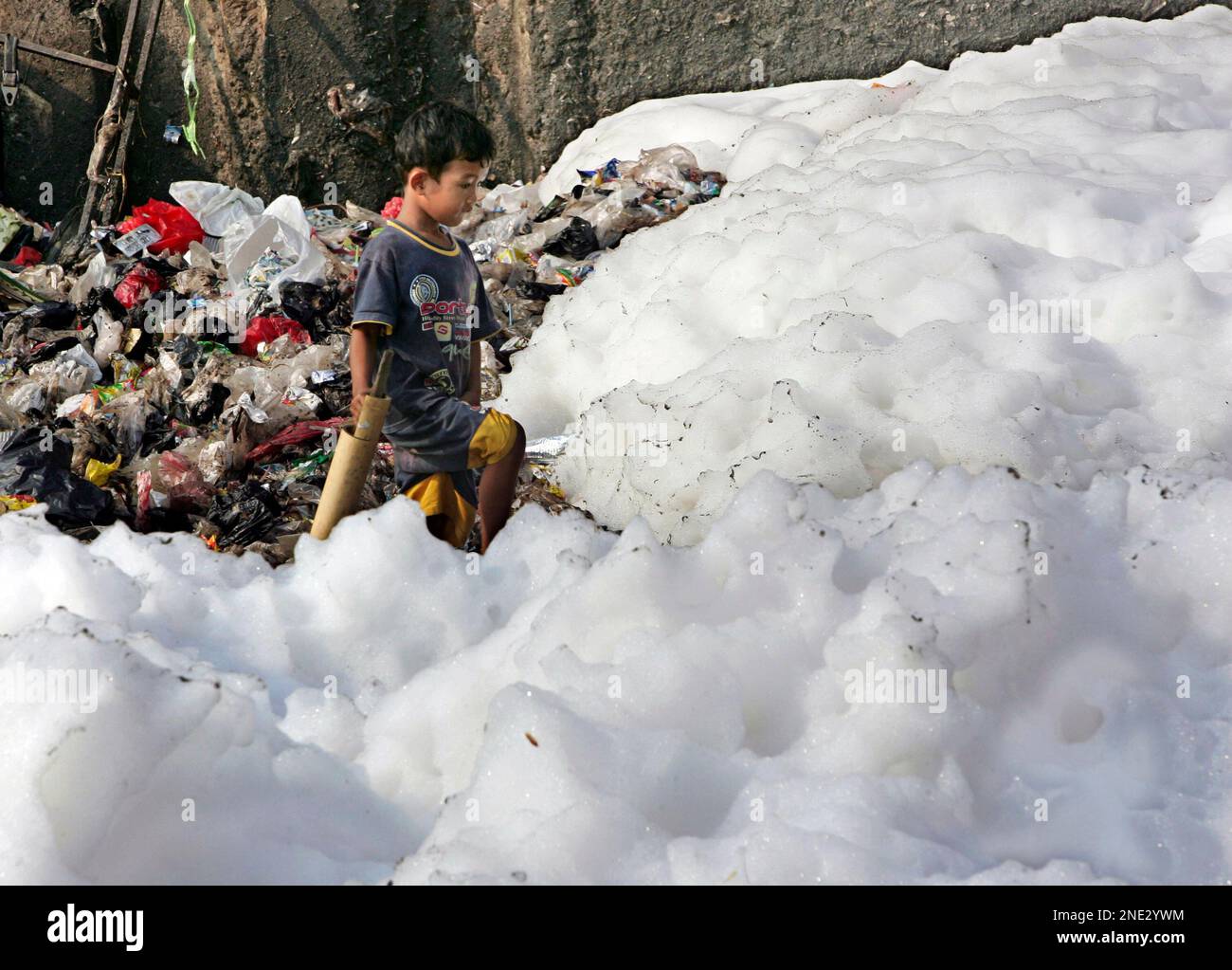 An Indonesian boy walks on a pile of garbage at a heavily polluted dam ...