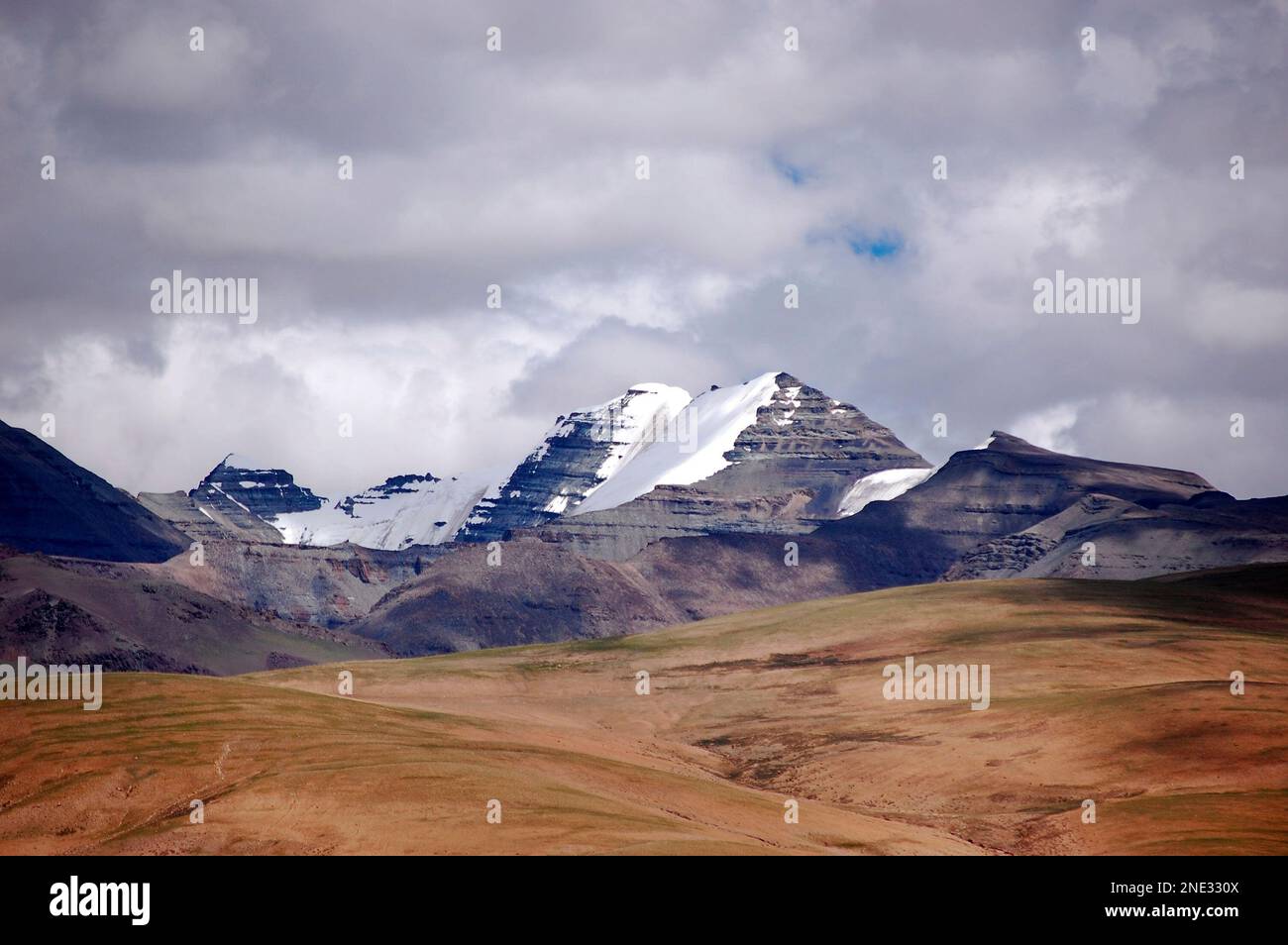 A low-angle of snowy Kangrinboqe peak with a yellow steppe view, cloudy ...