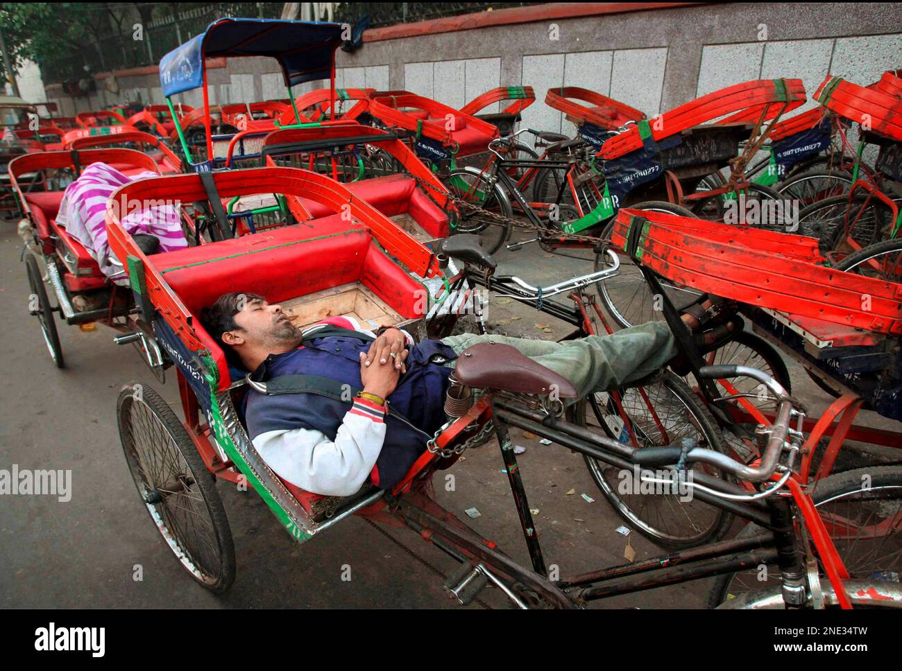 An Indian rickshaw driver sleeps as he waits for customers in New Delhi ...