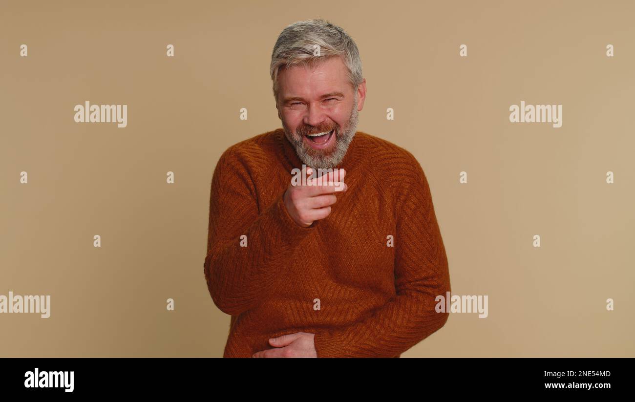 Amused middle-aged man pointing finger to camera, laughing out loud ...