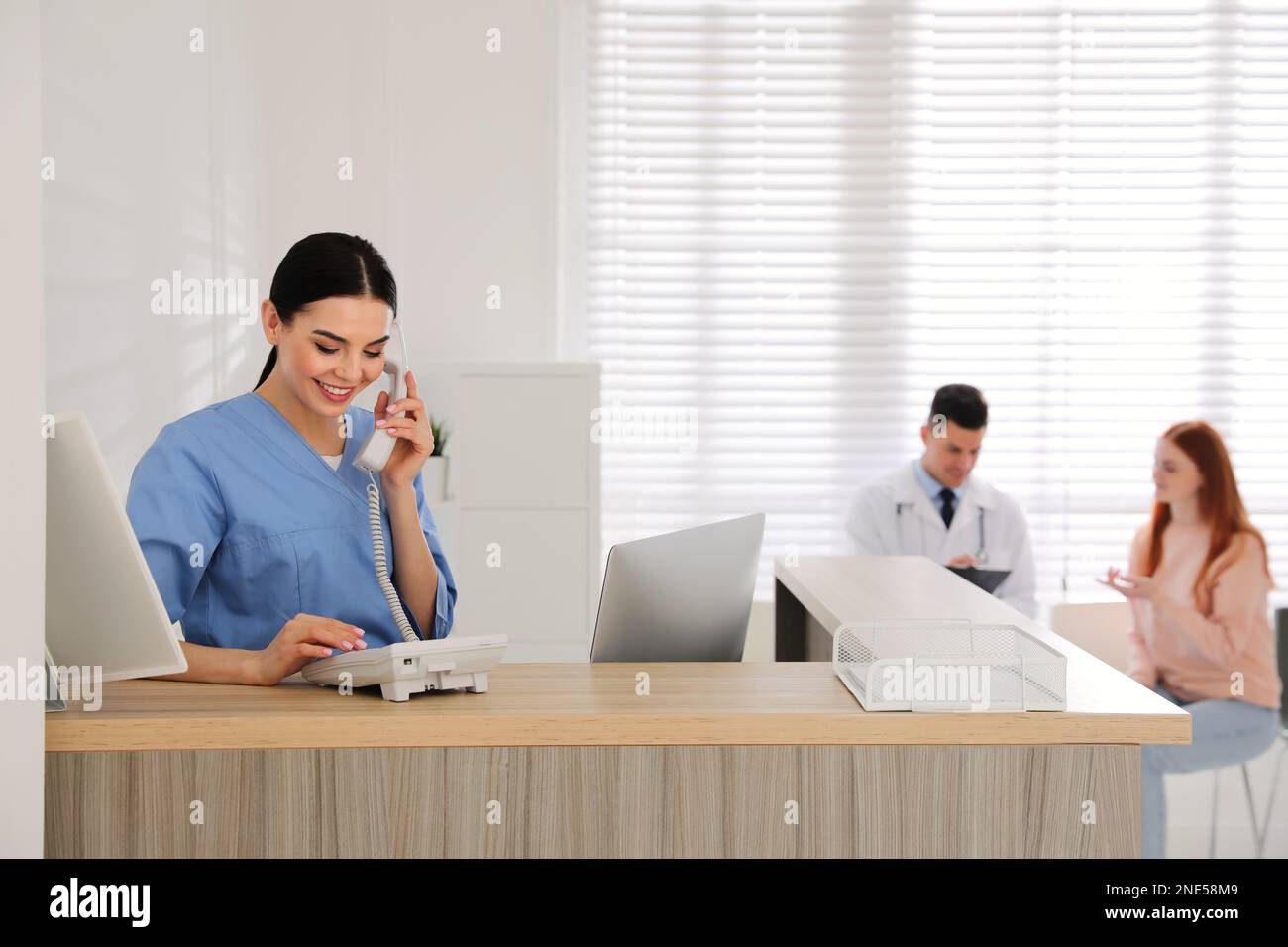 Receptionist talking on phone while doctor working with patient in ...