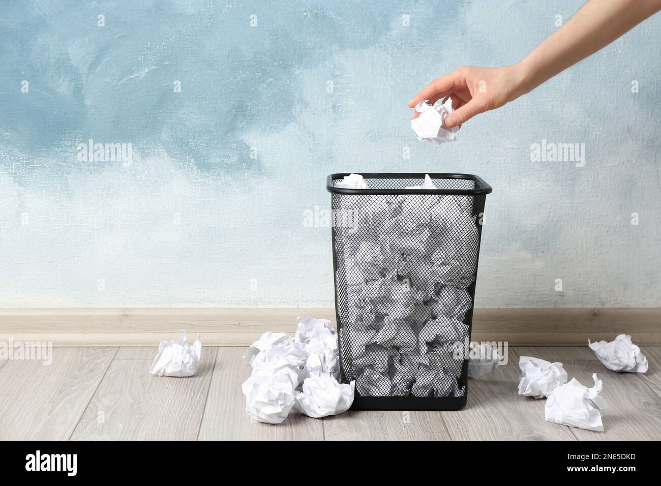 Woman throwing crumpled paper ball into basket near light blue wall ...