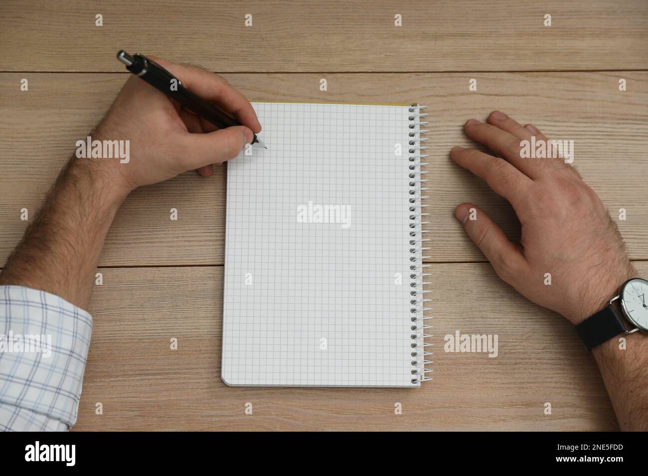 Left-handed man writing in notebook at wooden table, top view Stock ...