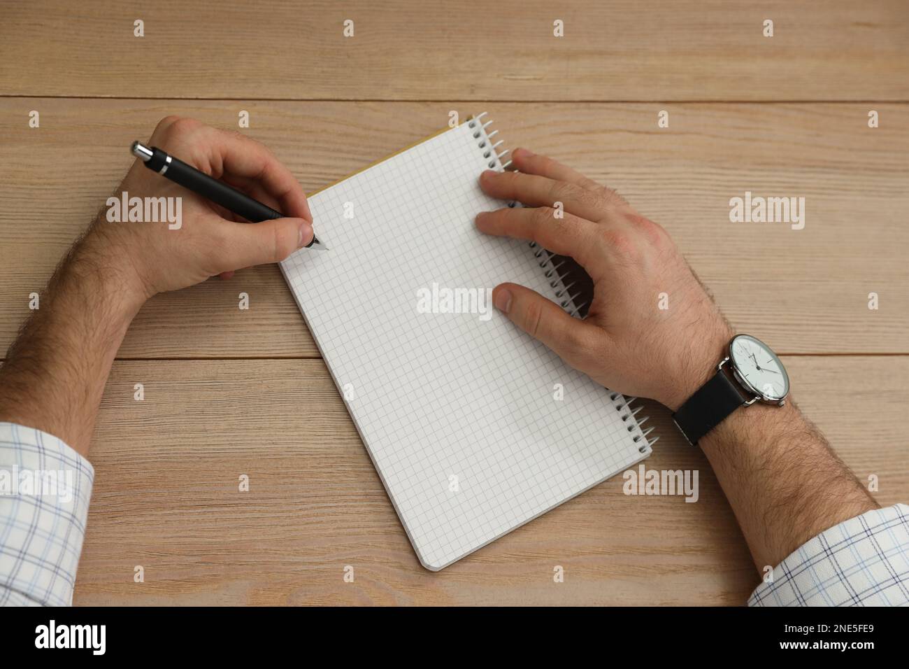 Left-handed man writing in notebook at wooden table, top view Stock ...