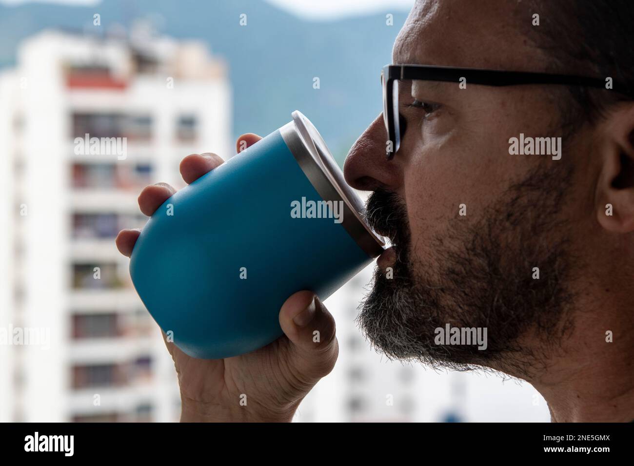 man drinking water from blue mug with view on blurred city background ...