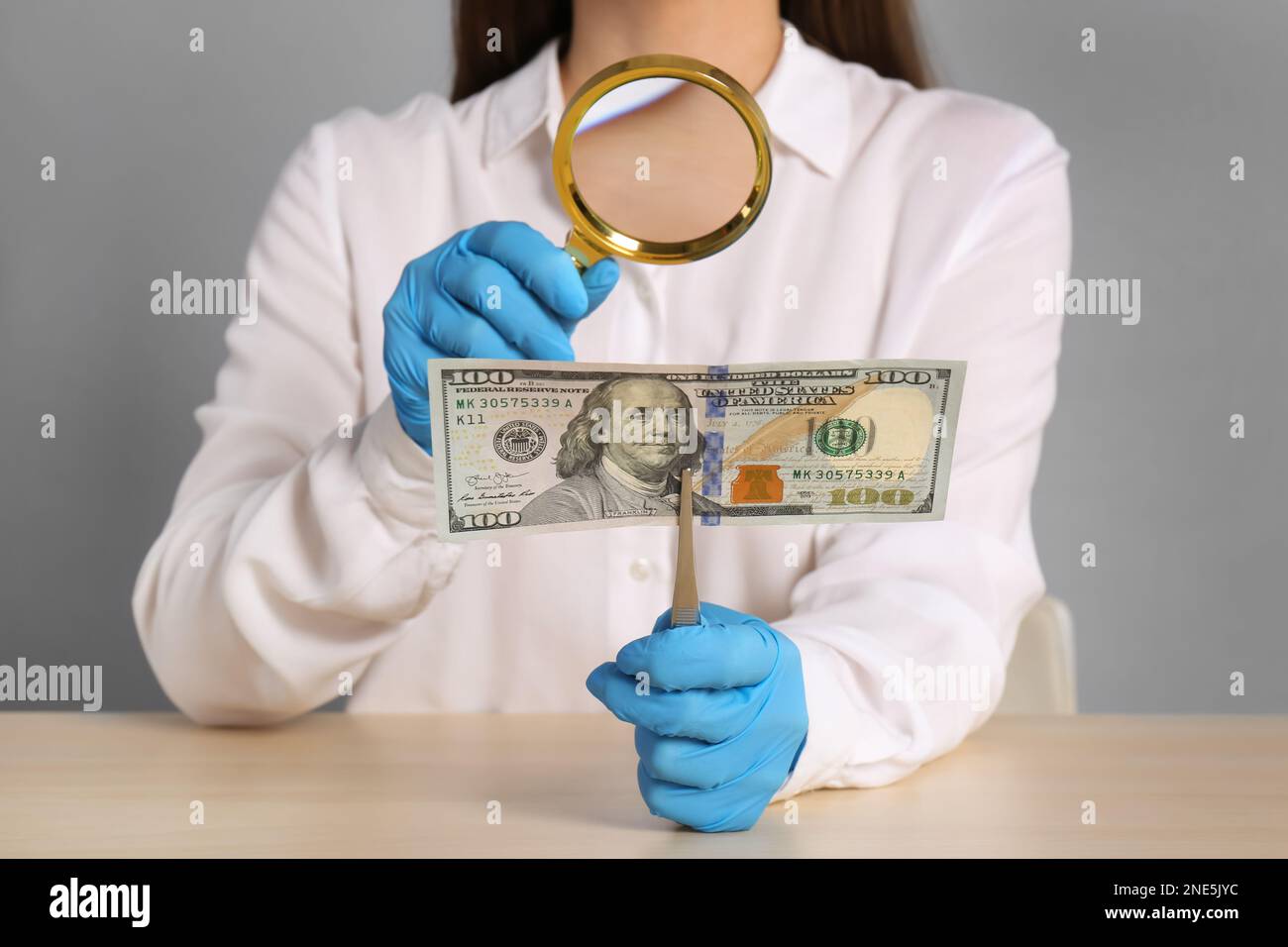 Expert authenticating 100 dollar banknote with magnifying glass at ...
