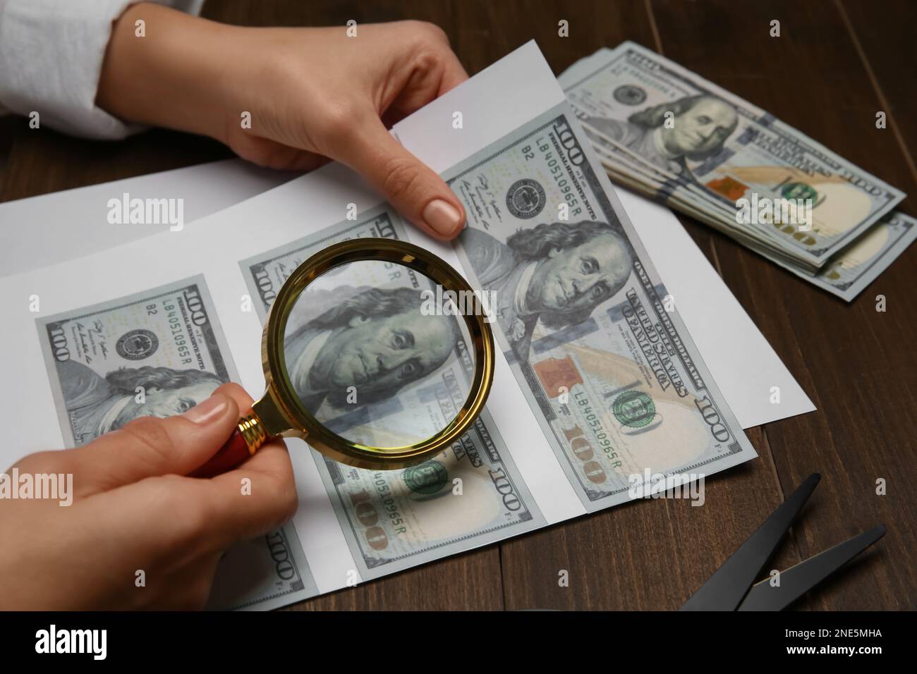 Counterfeiter examining sheet of paper with dollar banknotes at wooden ...