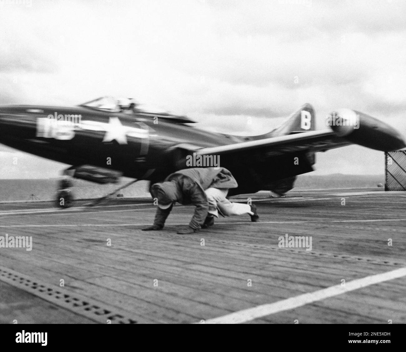 A Navy catapult crewman ducks as a Panther Jet streaks off the deck of ...