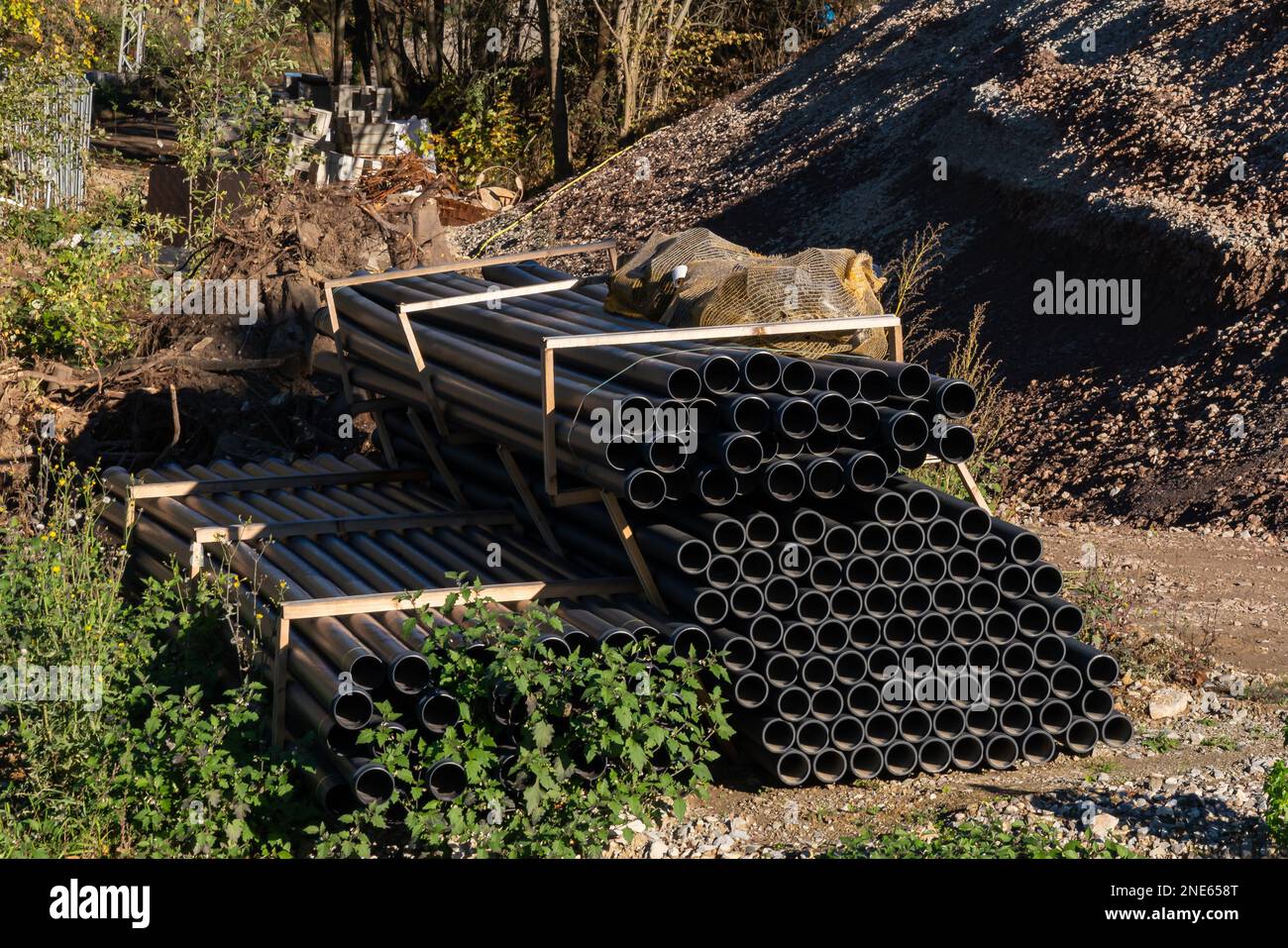 Bundles of black plastic pipes at a construction site overgrown with ...