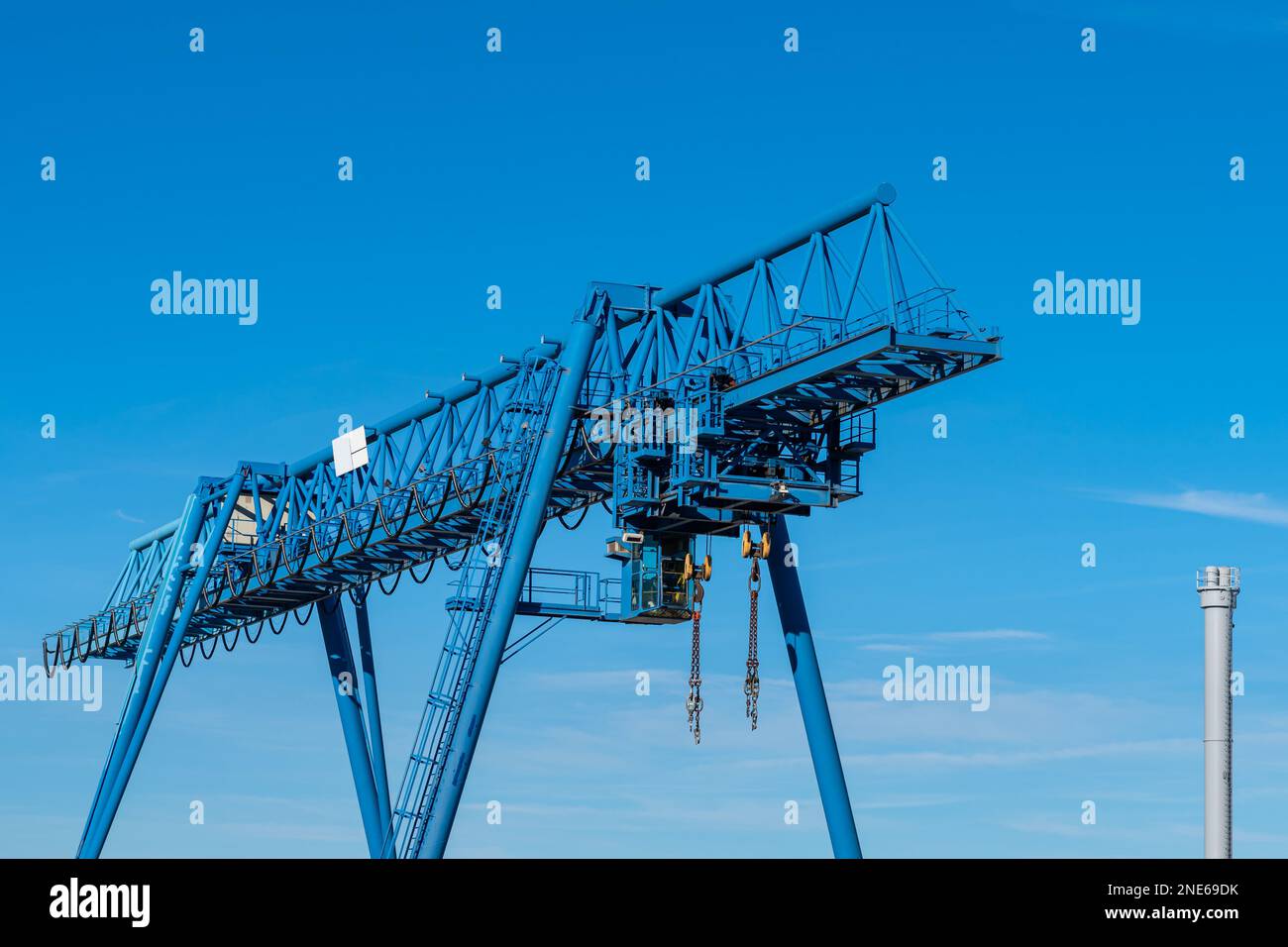 Blue overhead crane against a clear sky. On the right side is an ...