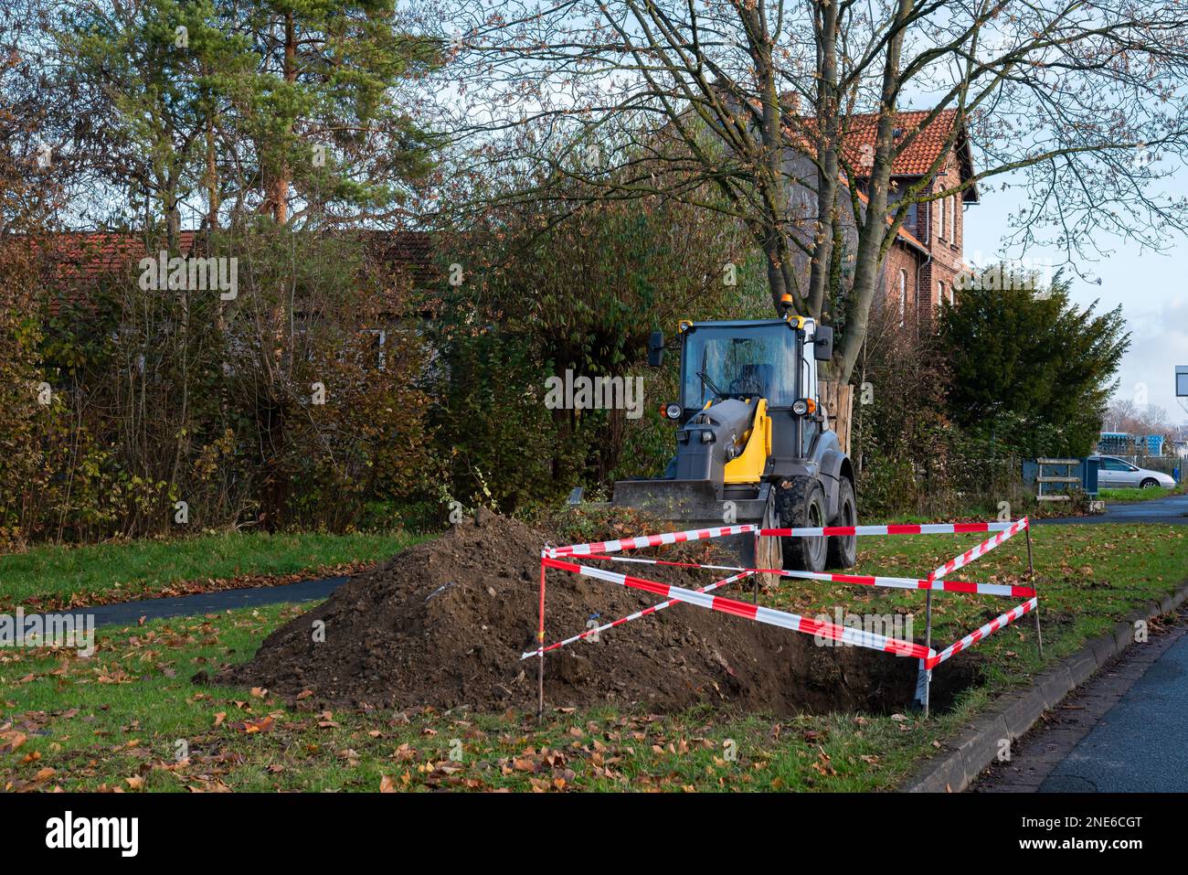 Yellow excavator next to a freshly dug hole fenced with red and white ...
