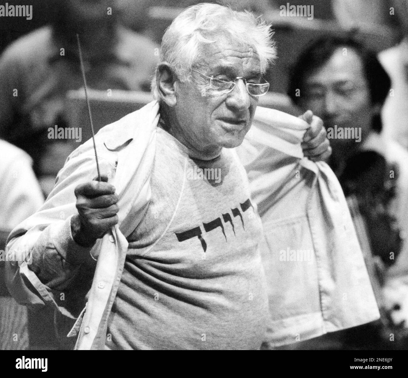 Conductor and composer Leonard Bernstein opens his shirt to display a t ...