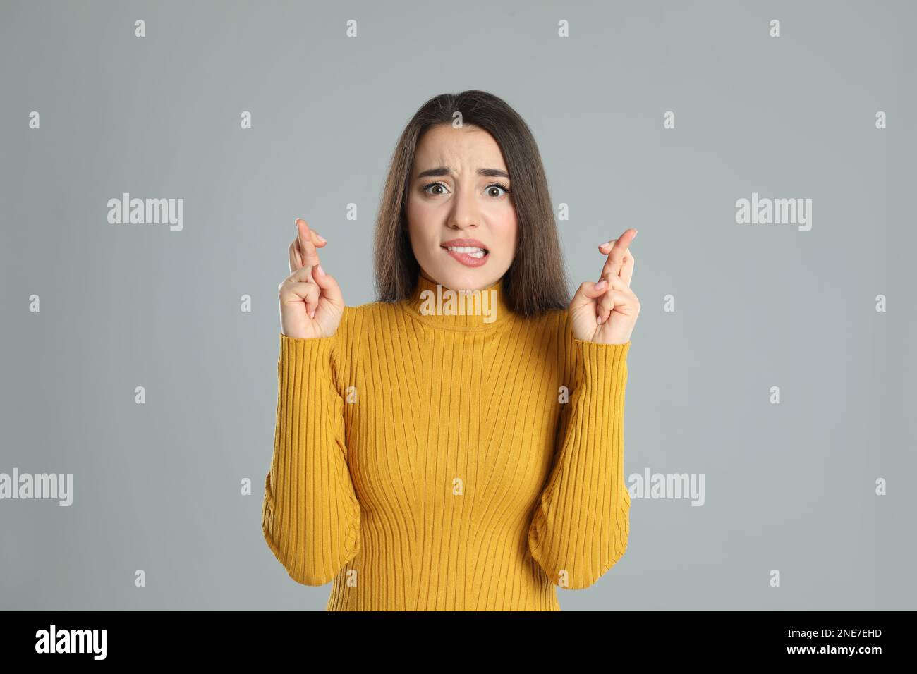 Nervous young woman holding fingers crossed on grey background ...