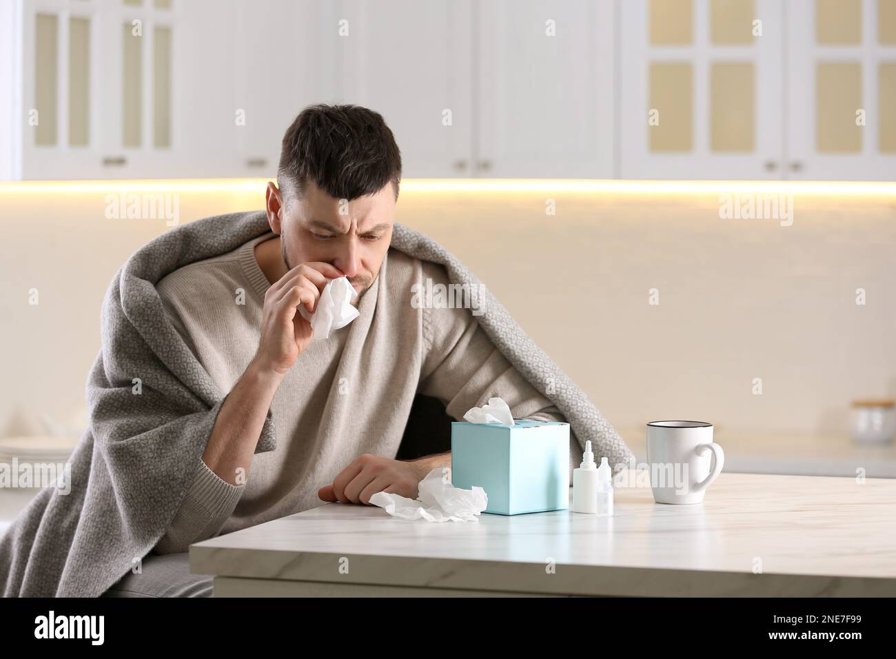 Ill man at table with nasal spray, drops and box of paper tissues in ...