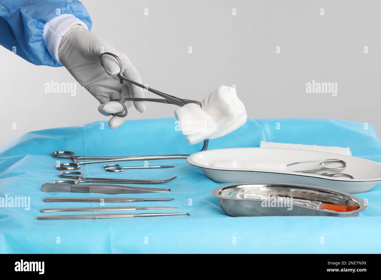 Doctor holding forceps with tissue over surgical instruments on table ...