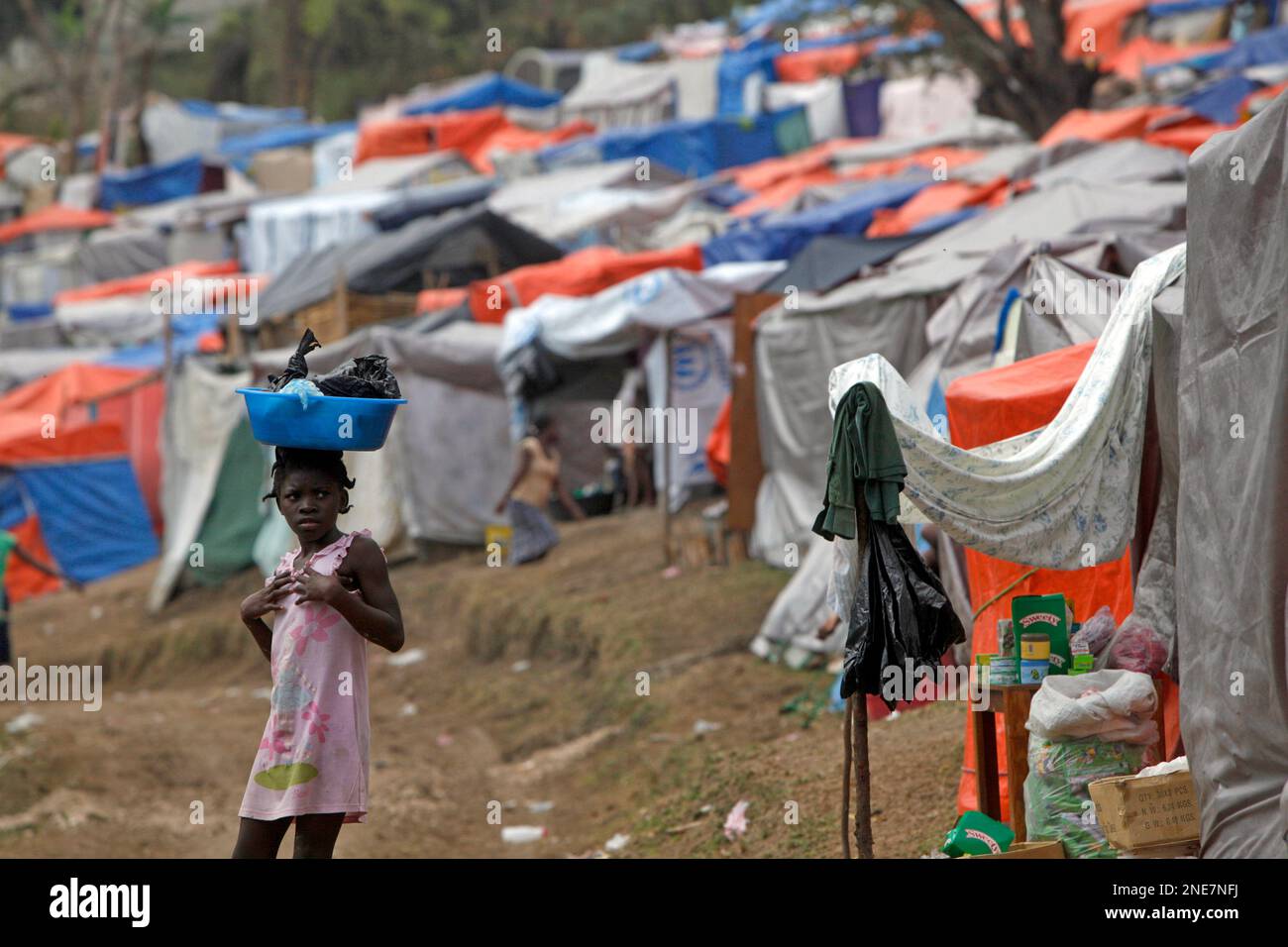A child carries a pail in her head as she walks inside a camp set up ...