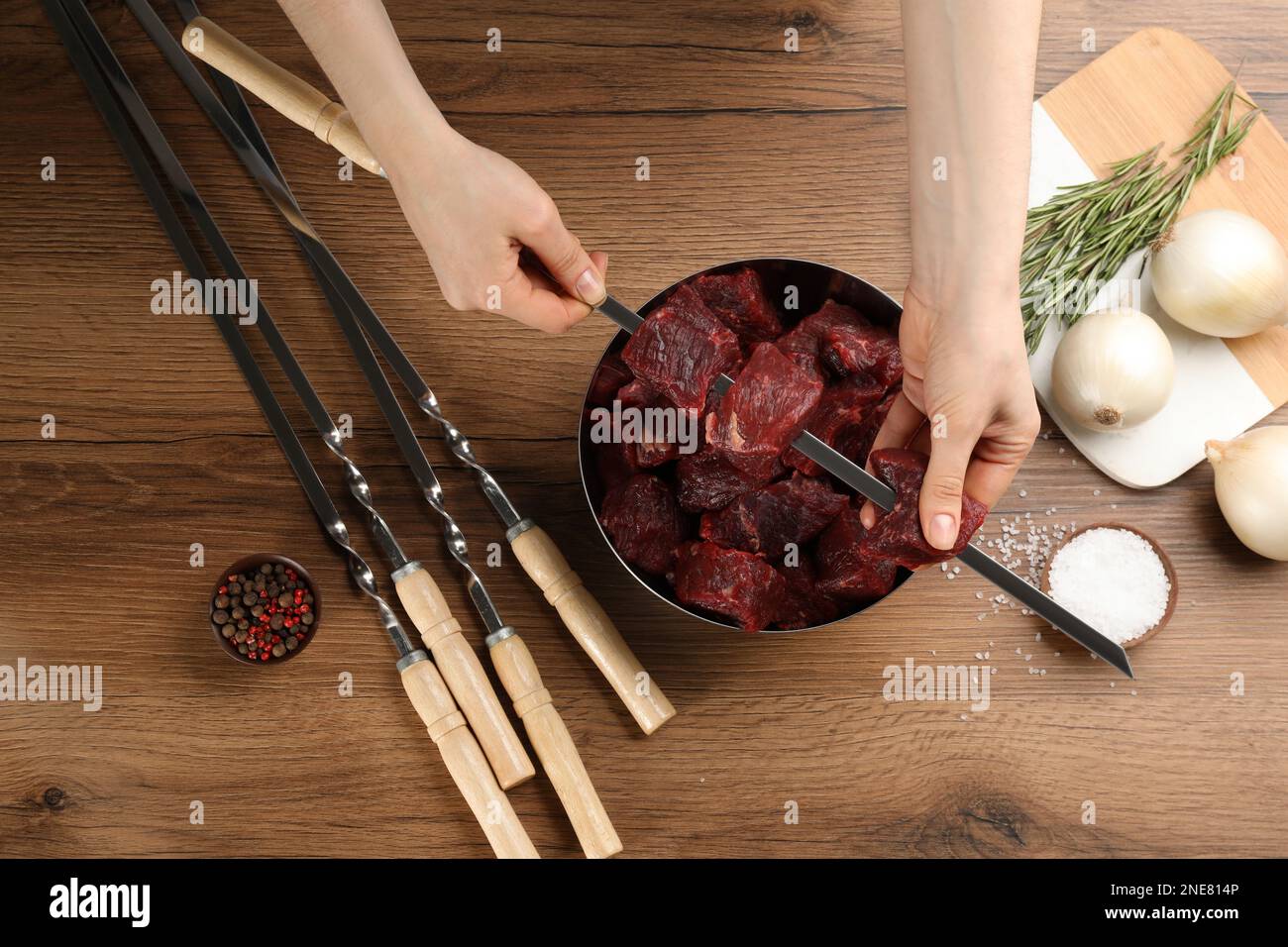 Woman stringing marinated meat on skewer at wooden table, top view ...