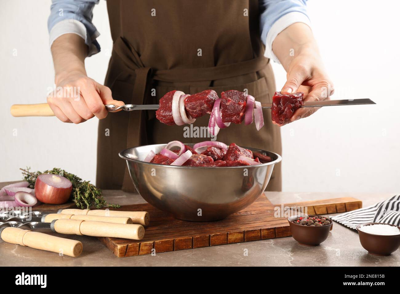 Woman stringing marinated meat and onion on skewer at table, closeup ...
