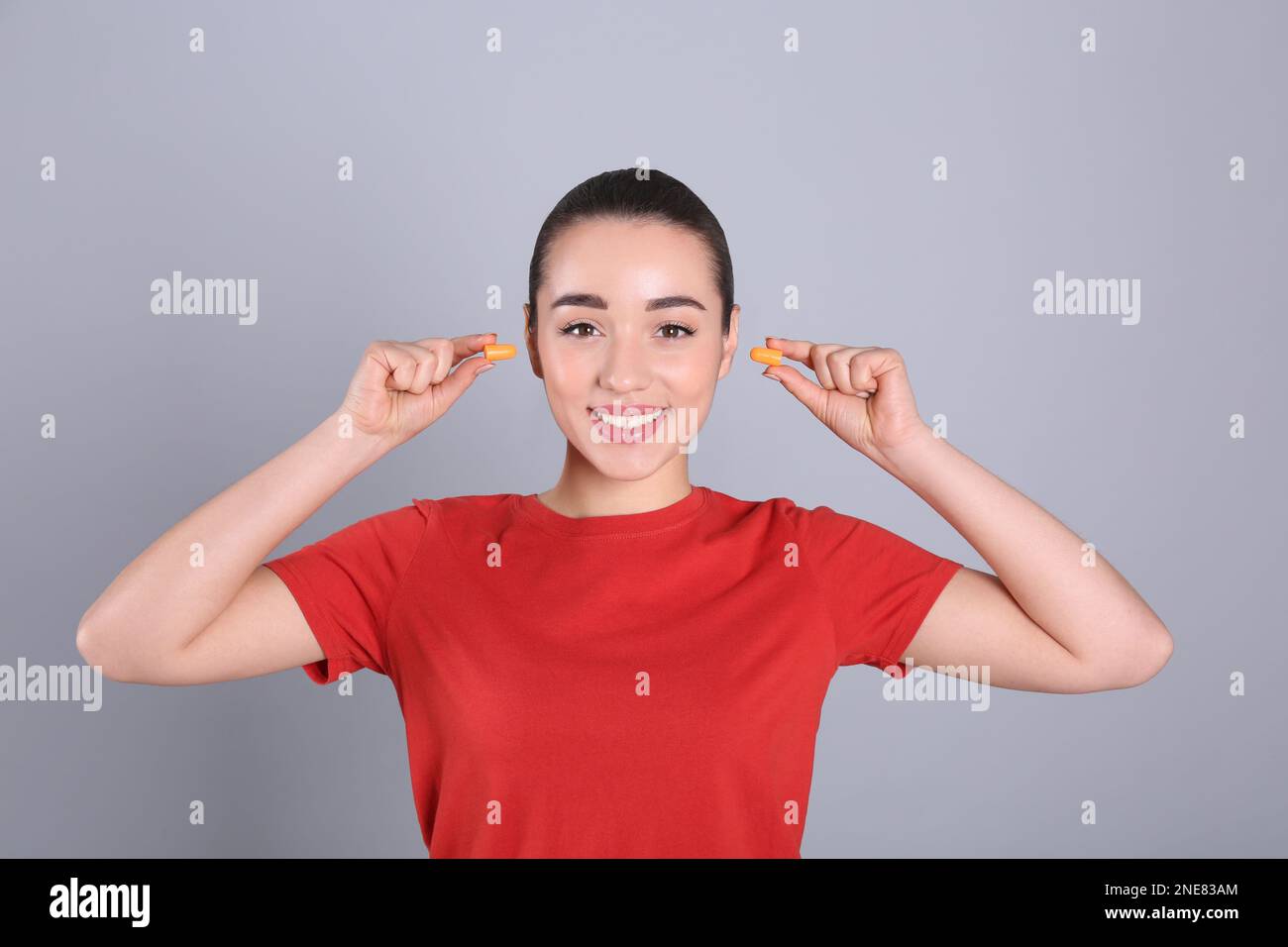 Young woman inserting foam ear plugs on grey background Stock Photo - Alamy