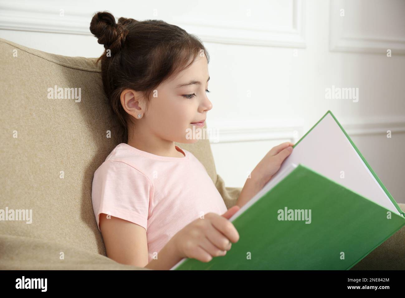 Little girl reading book in armchair at home Stock Photo - Alamy