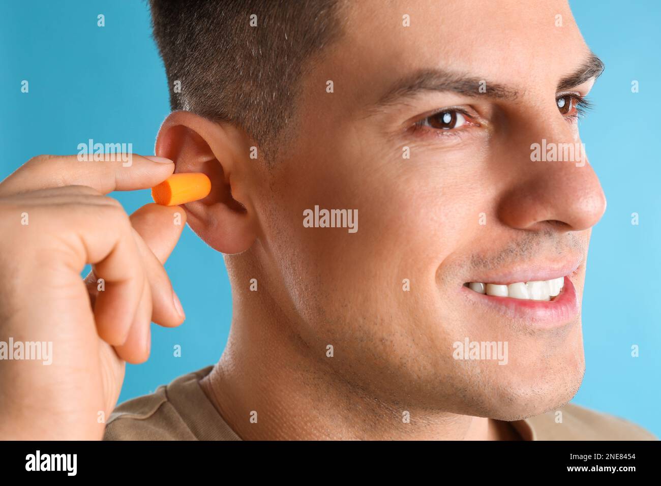 Man inserting foam ear plug on light blue background, closeup Stock ...