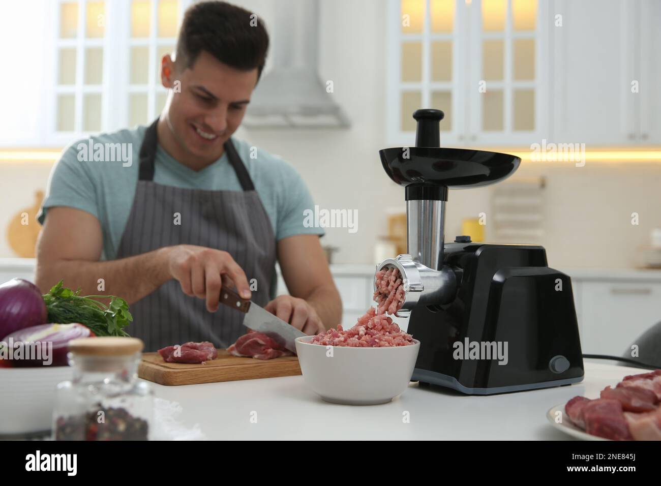 Man cutting meat in kitchen, focus on modern grinder Stock Photo - Alamy