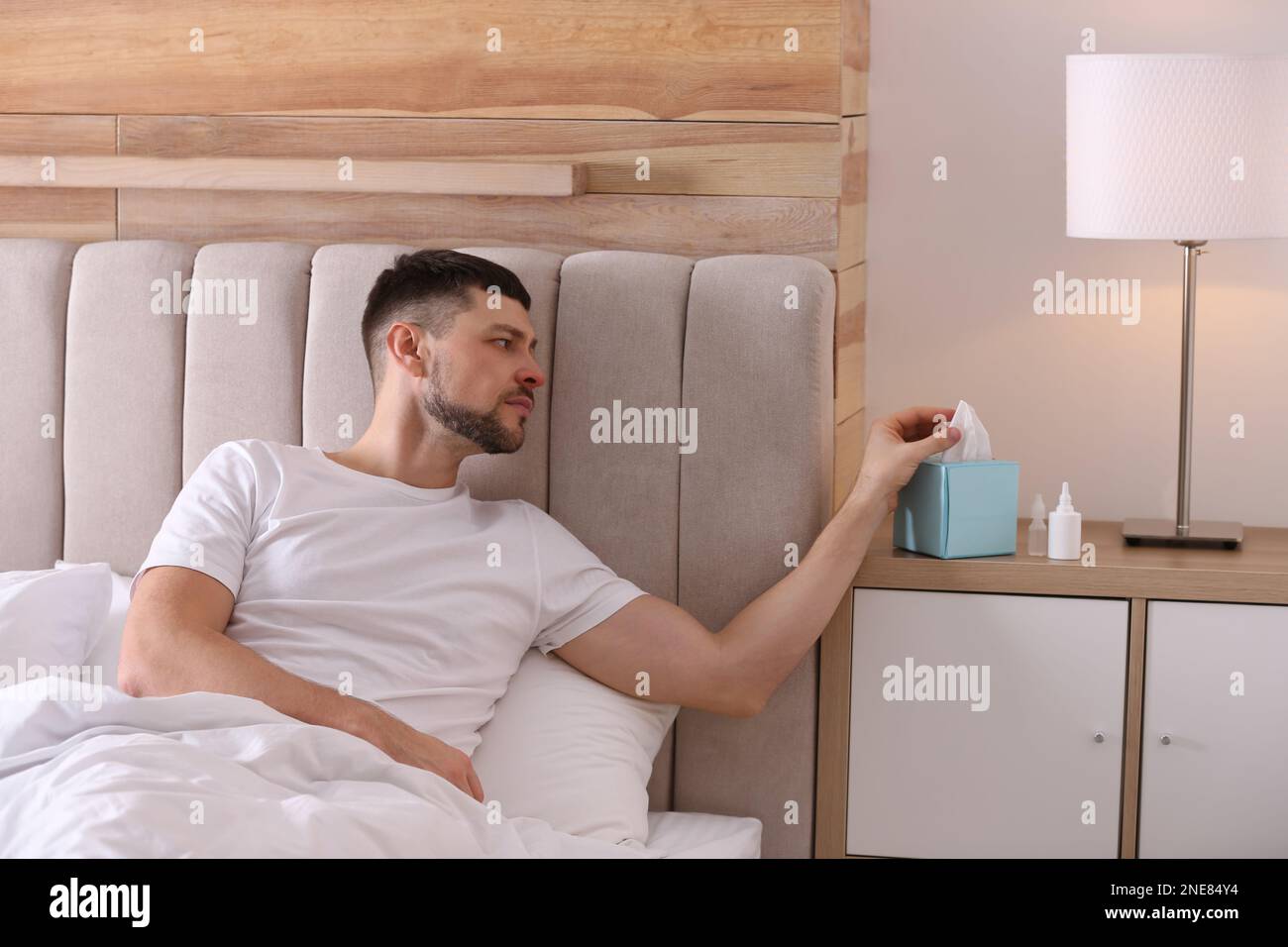 Ill man with nasal spray, drops and box of paper tissues in bed at home ...