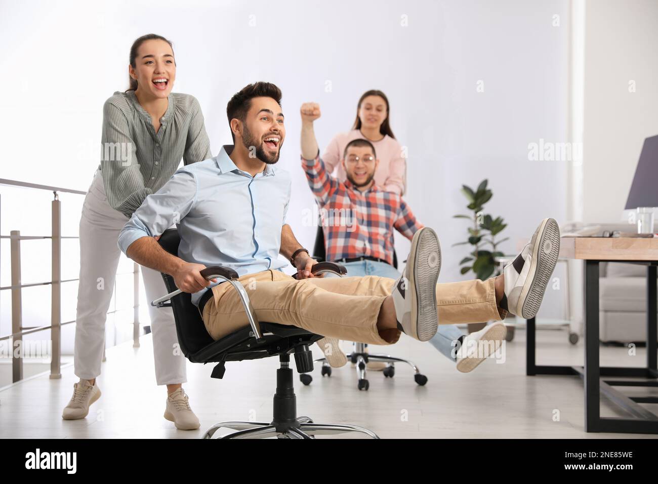 Happy office employees riding chairs at workplace Stock Photo - Alamy