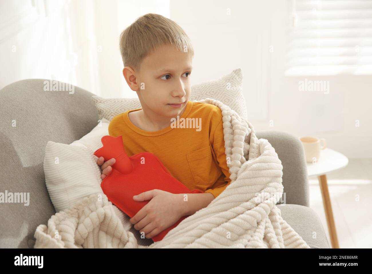 Ill boy with hot water bottle suffering from cold at home Stock Photo ...