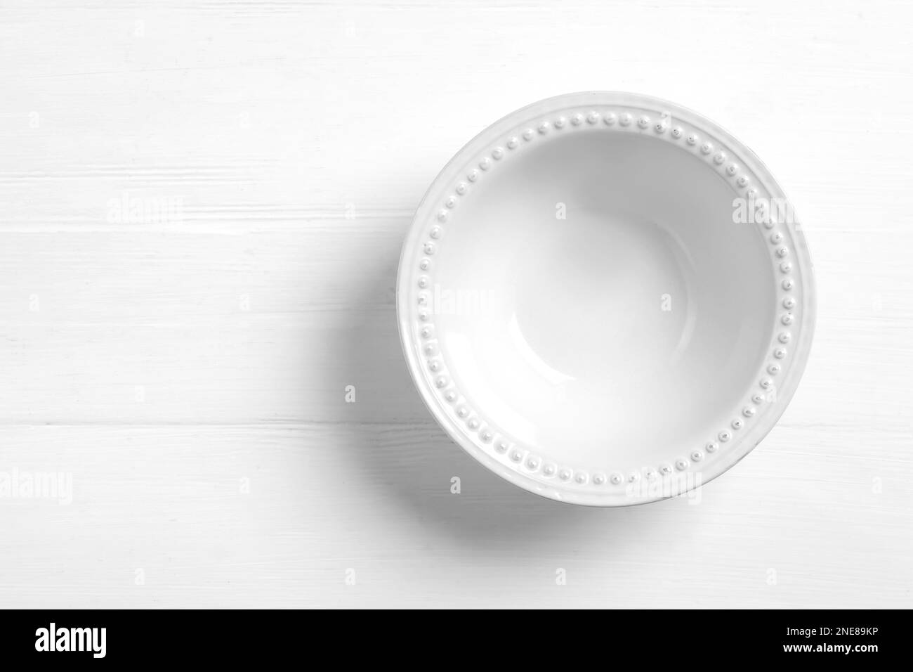Empty ceramic bowl on white wooden table, top view. Space for text ...