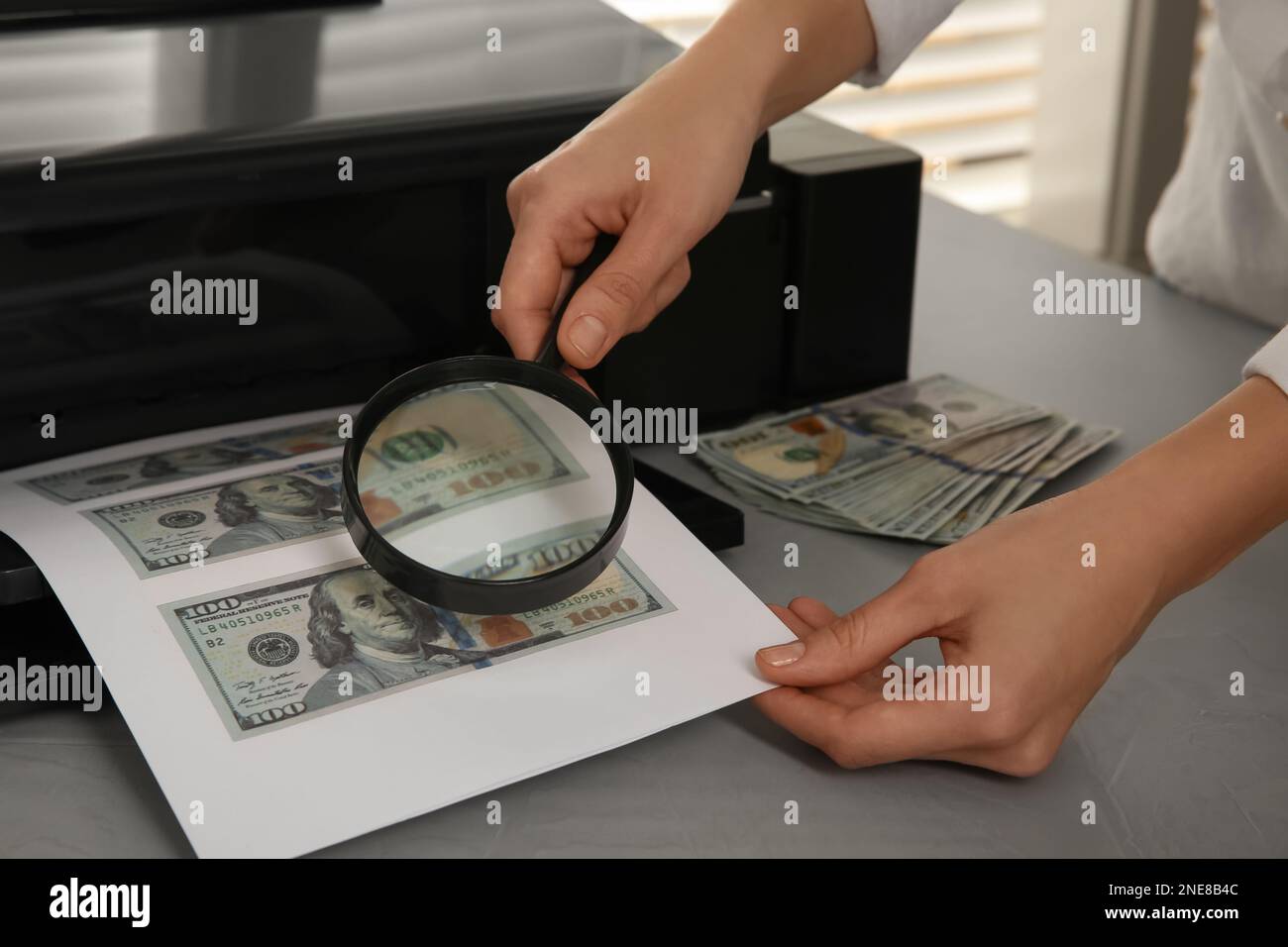 Counterfeiter examining sheet of paper with dollar banknotes at table ...
