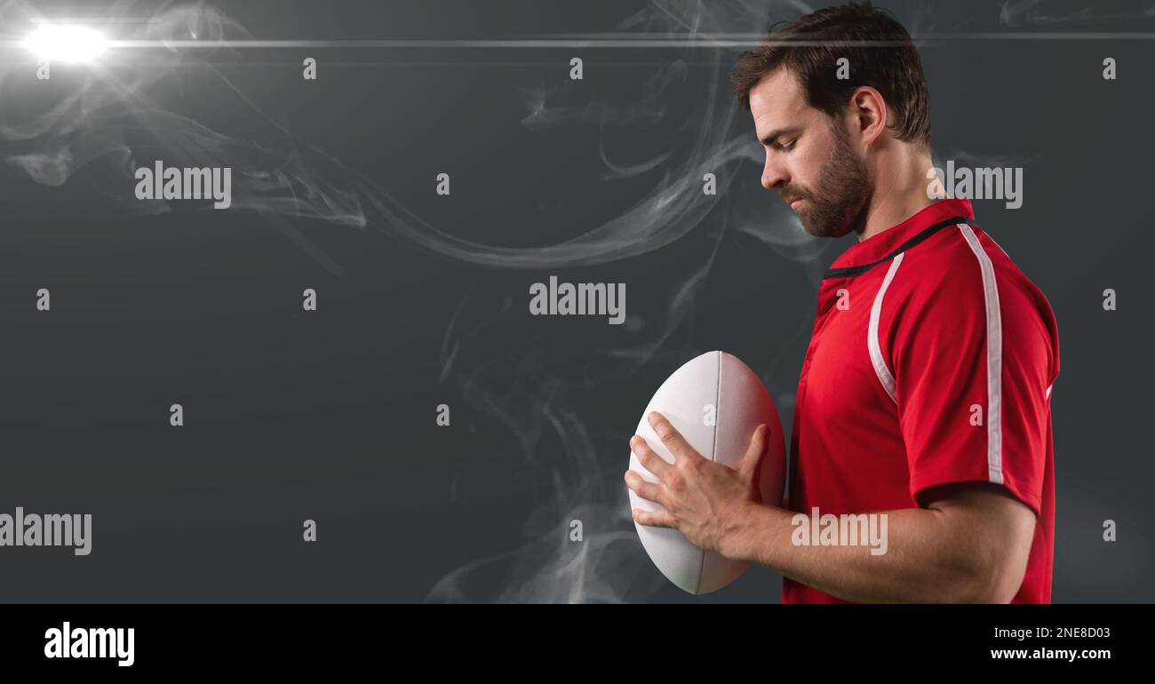 Caucasian male rugby player holding ball against smoke effect and light ...