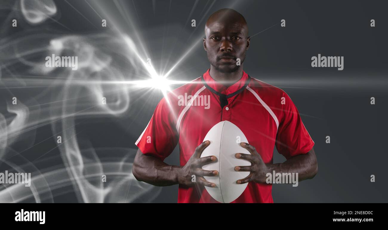 African american male rugby player holding ball against smoke and light ...