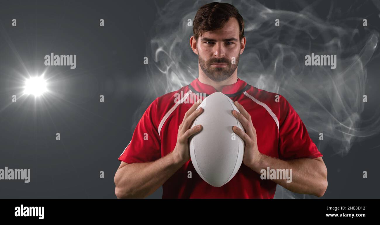 Portrait of caucasian male rugby player holding ball against smoke and ...