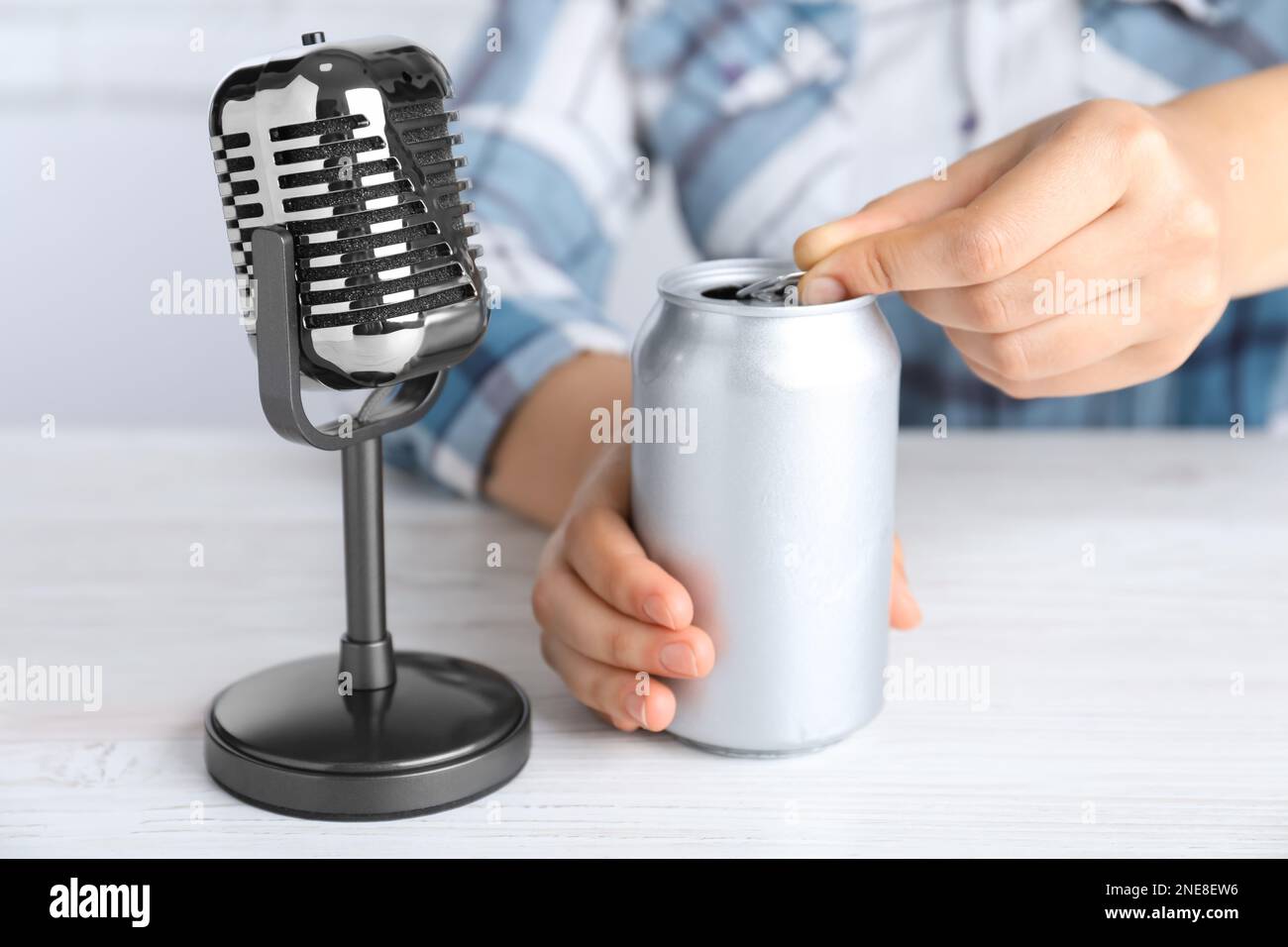 Woman making ASMR sounds with microphone and can at white table ...