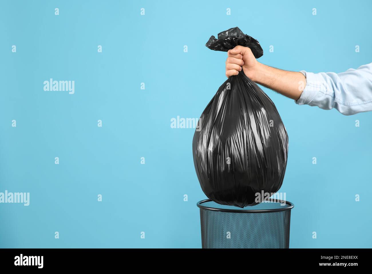 Woman taking garbage bag out of bin on light blue background, closeup ...