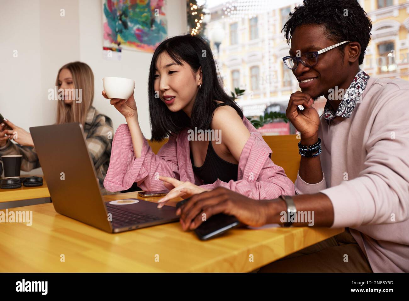 Happy multiethnic millennial friends sit in coffeeshop looking at ...