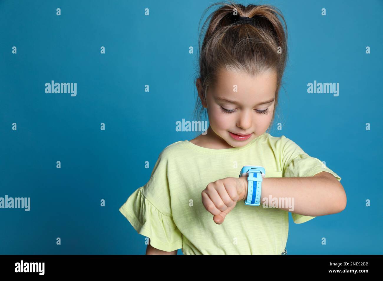 Little girl with smart watch on light blue background, space for text ...