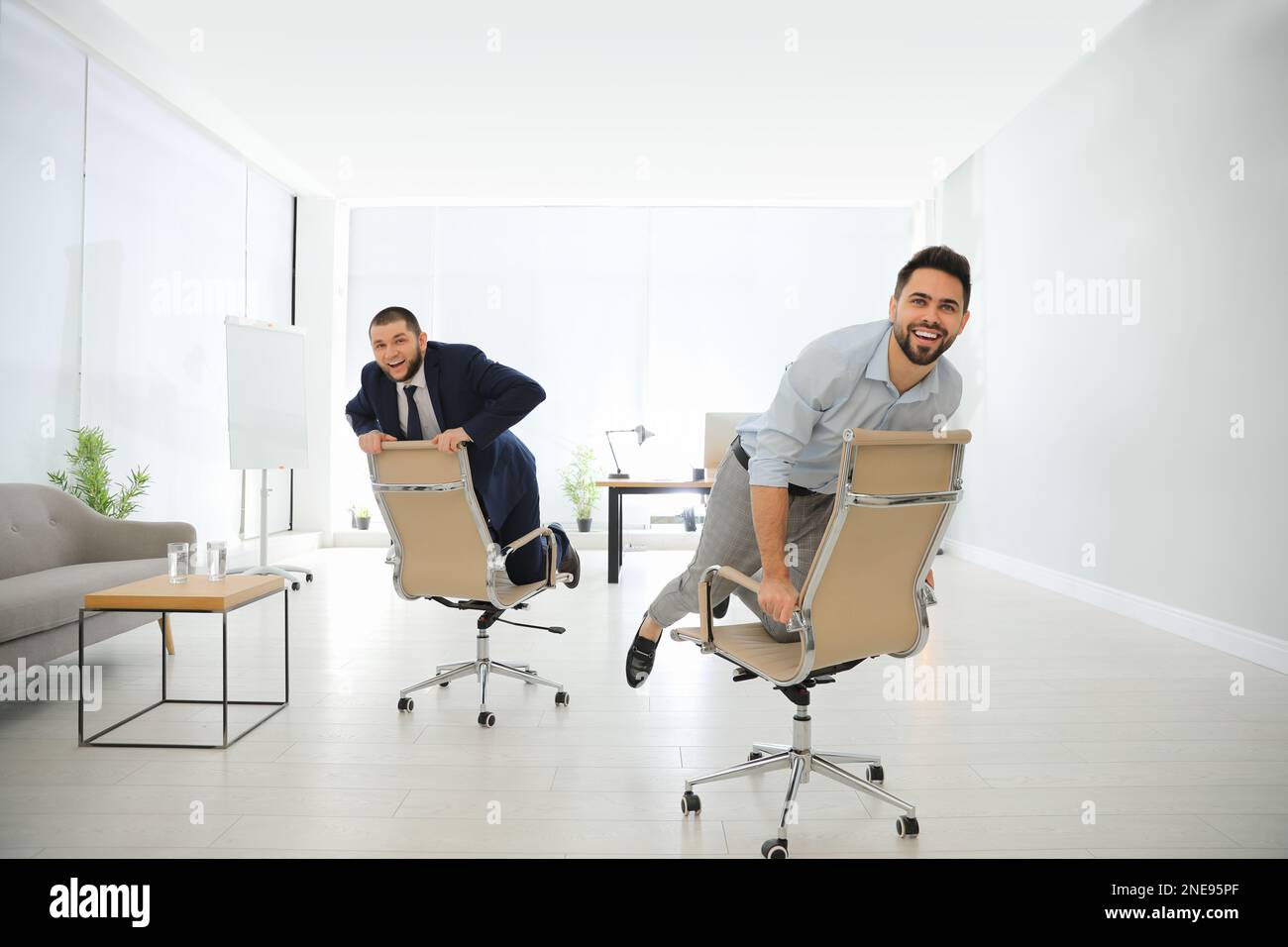 Happy office employees riding chairs at workplace Stock Photo - Alamy