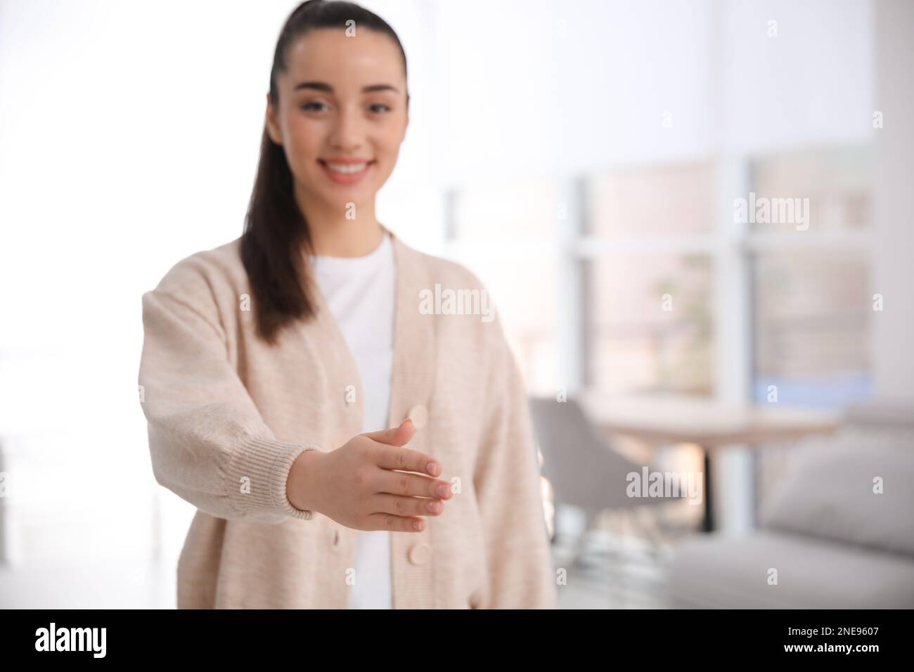 Happy young woman offering handshake indoors, focus on hand. Space for ...